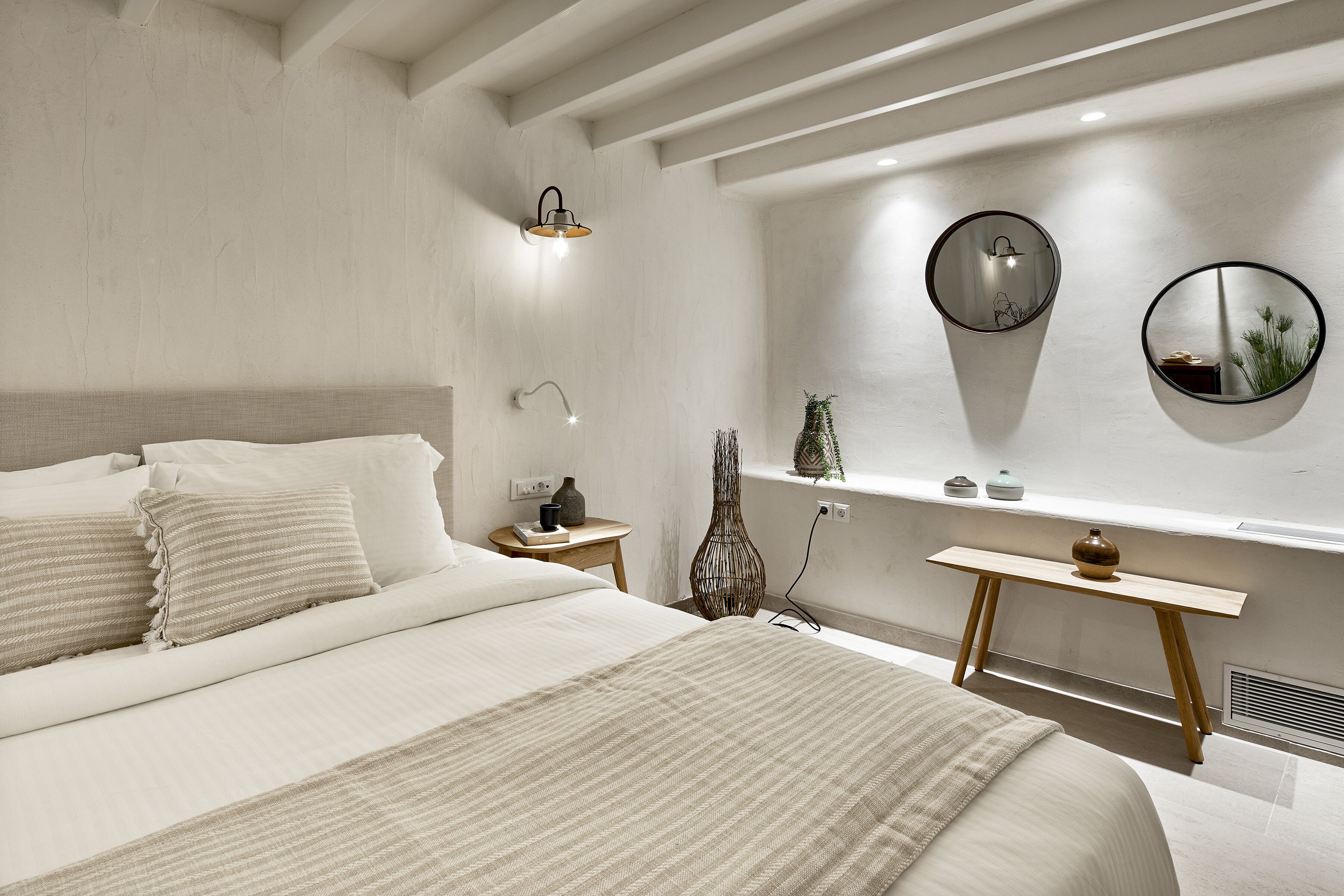 Quarto moderno com uma cama grande, mesas de cabeceira, toucador com espelhos e uma janela com vista.