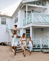 Uma família de quatro pessoas caminhando em direção a uma casa de dois andares com varanda e escada.