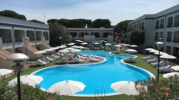 Uma piscina com espreguiçadeiras e guarda-sóis, rodeada por edifícios com varandas.