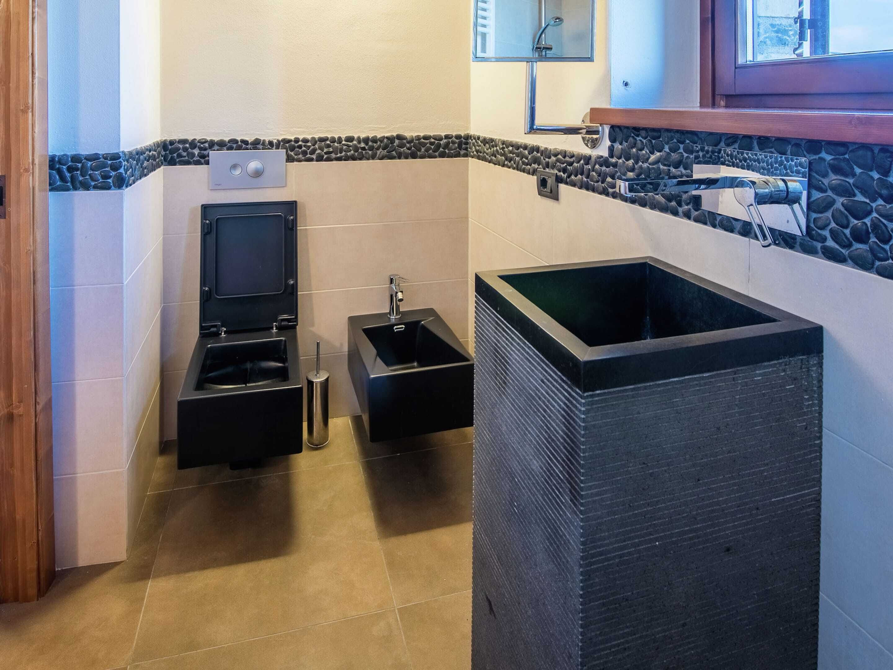 Uma casa de banho com sanita, lavatório e uma bacia preta grande.
