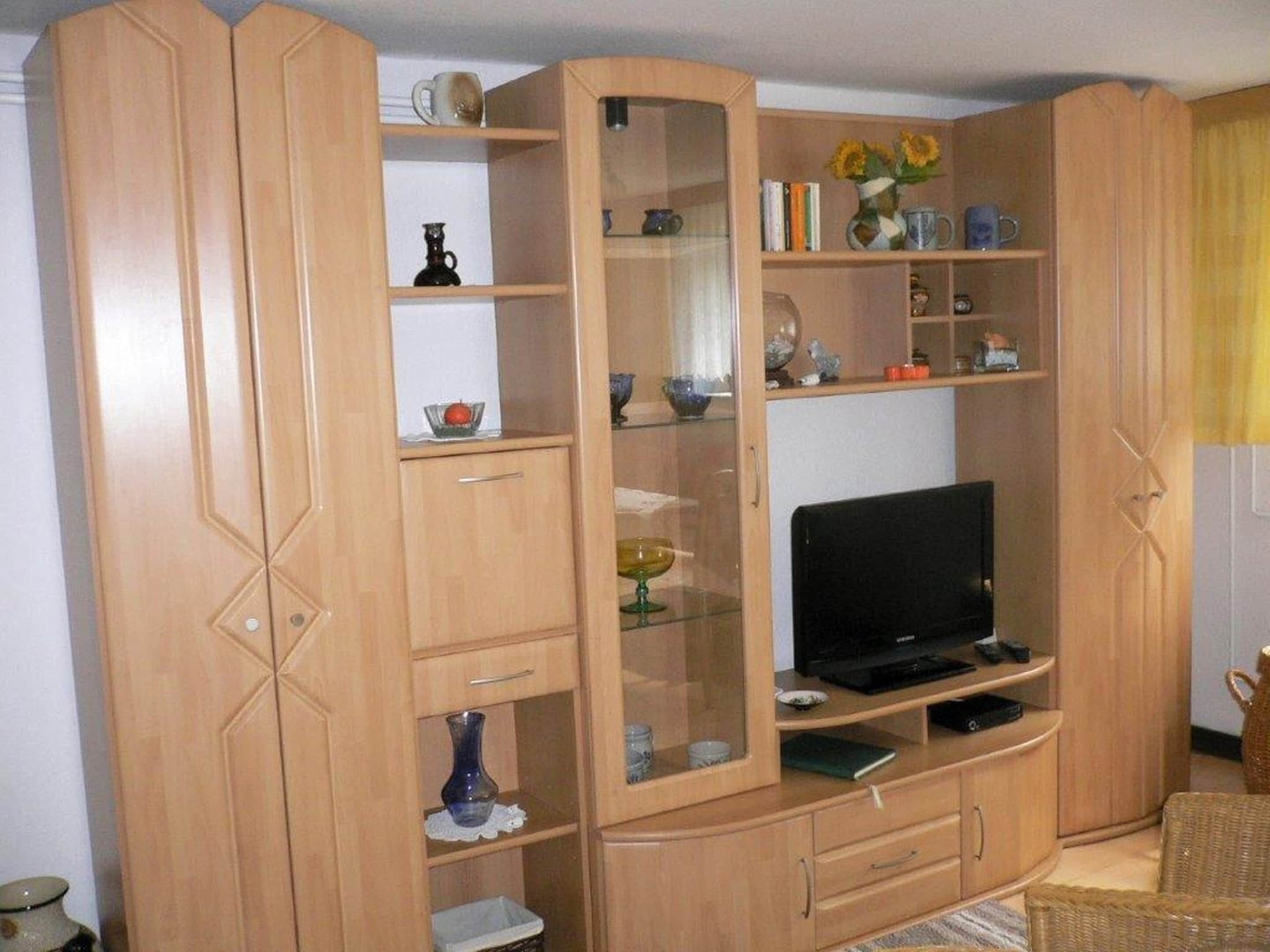 Sala de estar com um armário de madeira com prateleiras, uma televisão e diversos objetos decorativos.