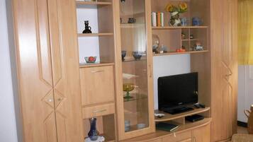 Sala de estar com um armário de madeira com prateleiras, uma televisão e diversos objetos decorativos.