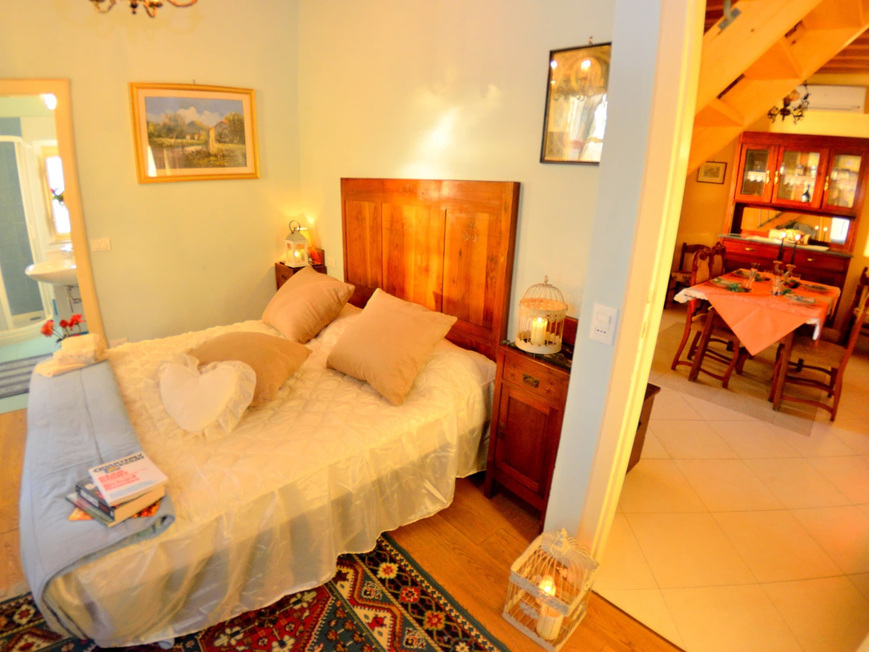 Quarto com cabeceira de madeira, cama com lençóis brancos, mesa de cabeceira com abajur e um tapete pequeno.