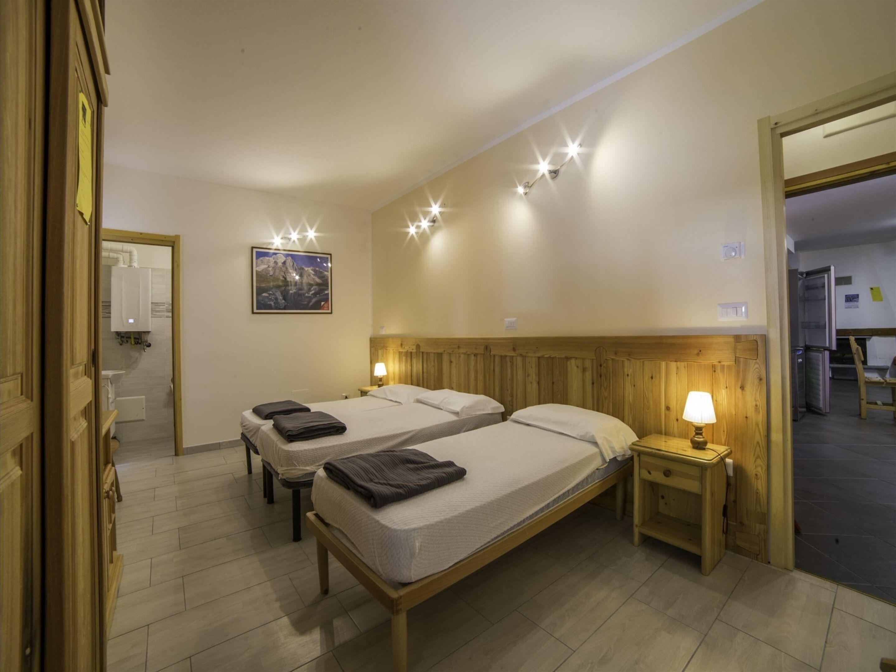 Quarto de hotel com duas camas, cabeceira de madeira, um quadro na parede e banheiro visível por uma porta aberta.