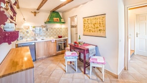Uma cozinha com vigas de madeira, chaminé verde, painel de azulejos e um quadro de cogumelos fixado na parede.