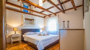 Quarto com teto de madeira, cama com lençóis brancos, mesa de cabeceira com abajur e espelho na parede.