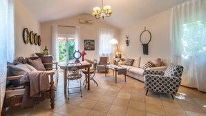 Sala de estar com sofá, poltrona, mesa de jantar e lustre.