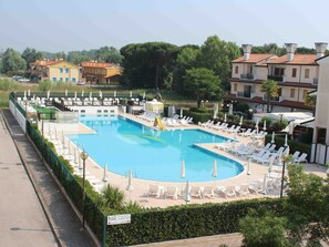 Piscina com espreguiçadeiras e guarda-sóis, cercada por vegetação e edifícios.