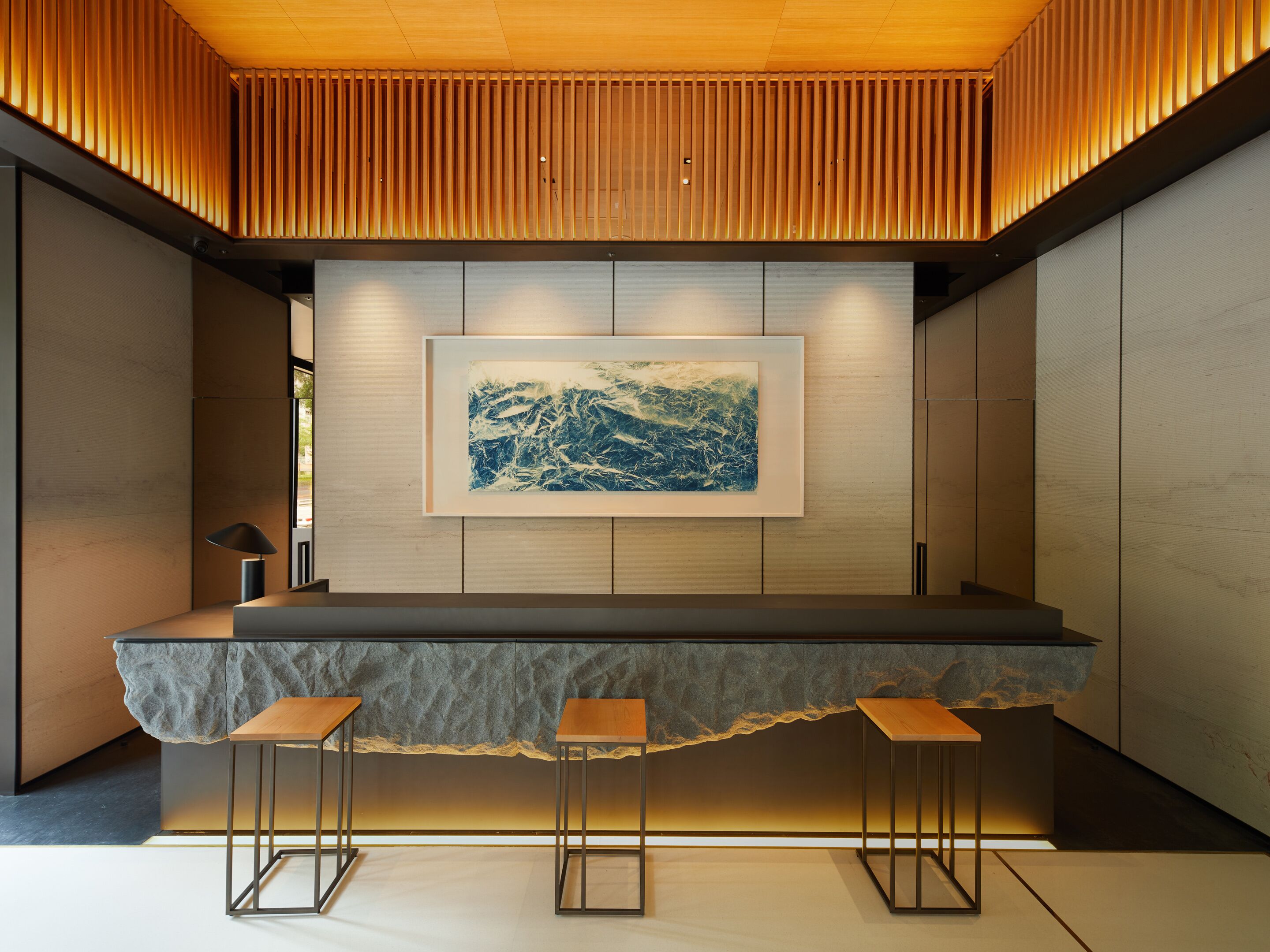 Um bar moderno com teto de ripas de madeira, uma pintura abstrata emoldurada e três banquetas.