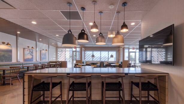 Uma área de bar moderna com um balcão comprido, várias luminárias pendentes e banquetas.