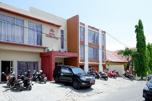 Um hotel com várias motocicletas estacionadas na frente, um SUV preto e um carro vermelho.