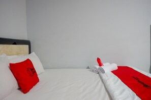 Cama bem arrumada com roupa de cama branca e manta vermelha.