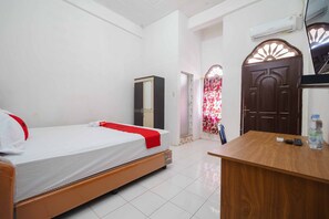 Quarto de hotel com cama, escrivaninha de madeira, ar condicionado e guarda-roupa.