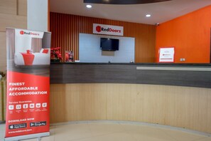 Balcão de recepção RedDoorz com uma TV de tela plana, um aviso de garantia de serviço e um cartaz de download agora.