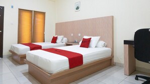 Quarto de hotel com duas camas de solteiro, cada uma com uma almofada vermelha decorativa, uma cabeceira de madeira e uma mesa de cabeceira.