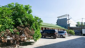 Uma área de estacionamento pavimentada, com uma árvore e um edifício com telhado verde.