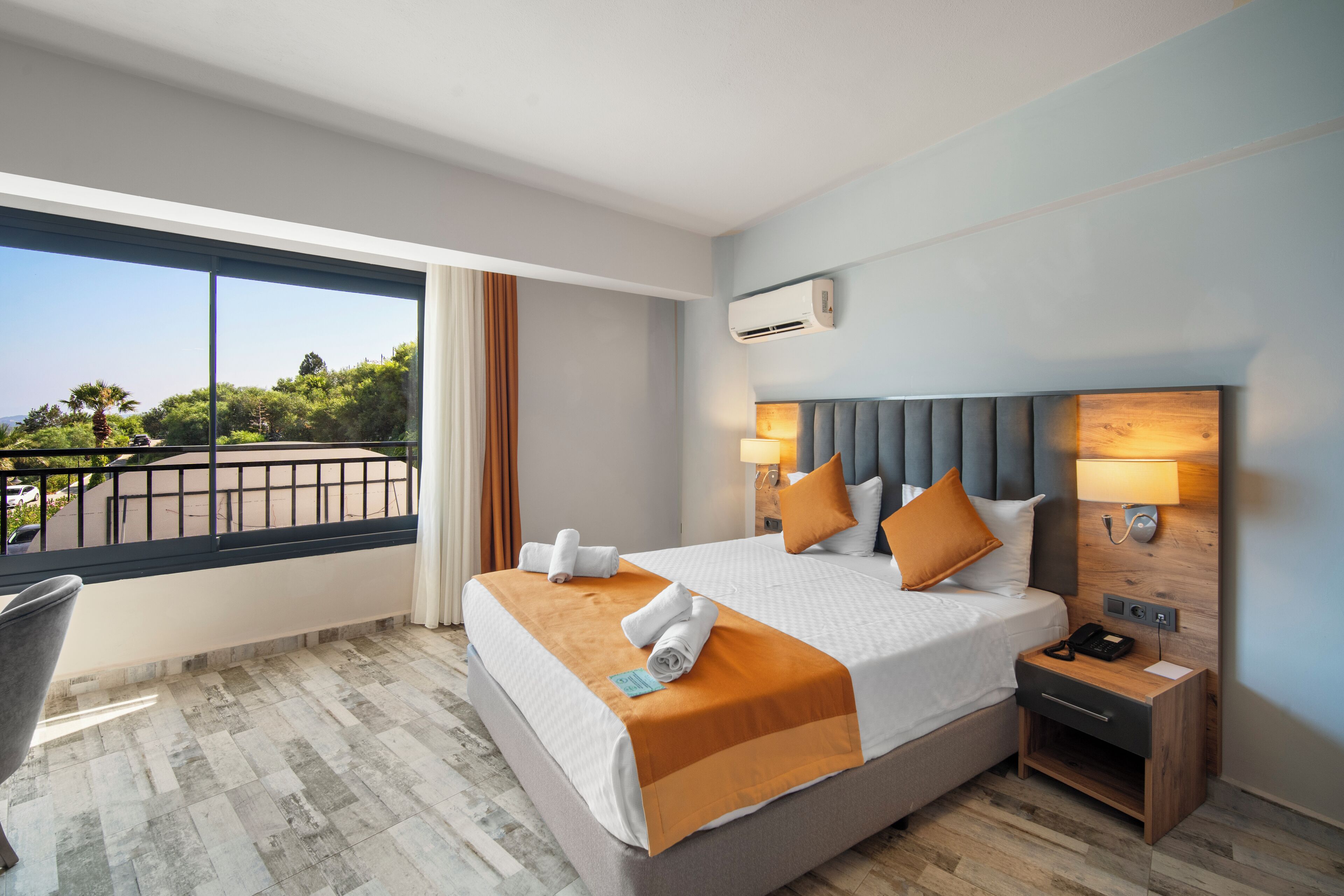 Quarto de hotel com cama grande, mesa de cabeceira, luminária e vista para o exterior.