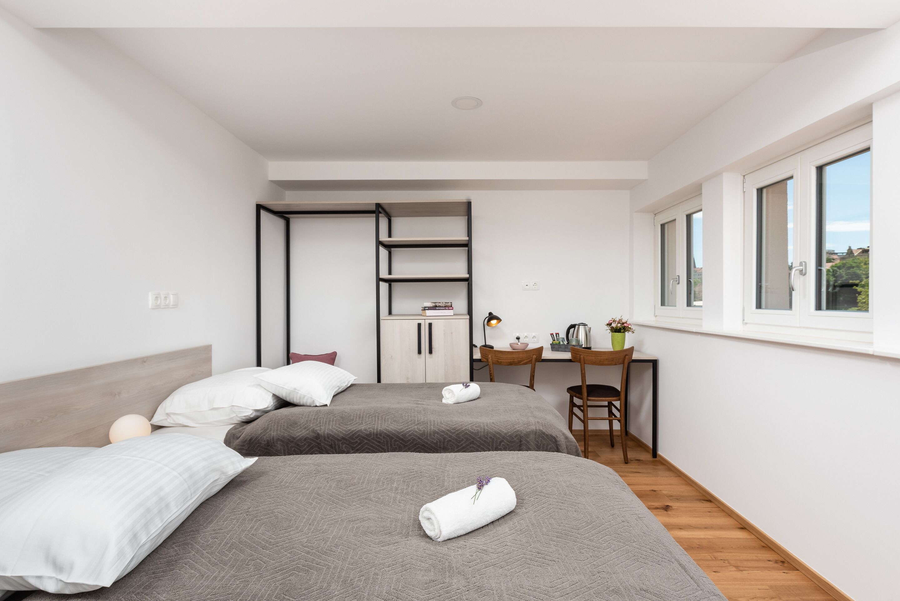 Quarto moderno e minimalista com duas camas, uma escrivaninha e uma janela.