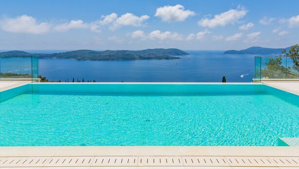 Piscina azul e límpida com vista para o mar e ilhas ao longe.