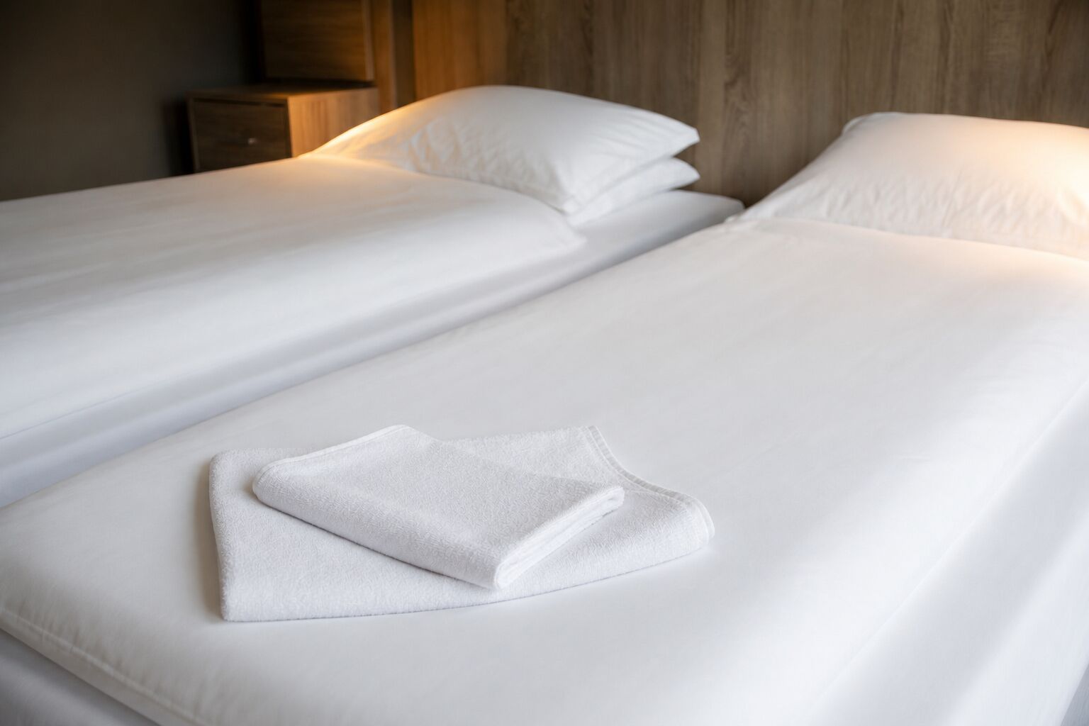 Cama bem arrumada com lençóis brancos e uma toalha dobrada sobre ela.