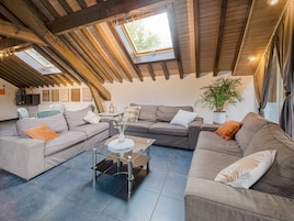Uma sala de estar estilo loft com vigas de madeira aparentes, um sofá modular, uma mesa de centro de vidro e um vaso com planta.