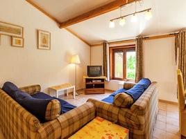 Uma sala de estar acolhedora com dois sofás xadrez, uma mesinha, um abajur e uma televisão sobre um móvel de madeira.