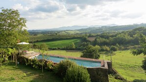 Piscina rodeada por vegetação exuberante e campos, com vista para colinas distantes.