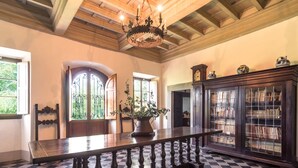Um quarto com piso xadrez, uma mesa de madeira com corrimão, um candelabro e um armário com portas de vidro.