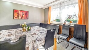 Uma área de refeições com uma mesa posta para quatro pessoas, cadeiras pretas, um vaso com flores e um quadro na parede.
