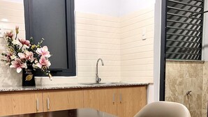 Uma mesa de jantar com três copos de vidro transparente, um vaso com flores cor-de-rosa e um armário preto sobre a pia.