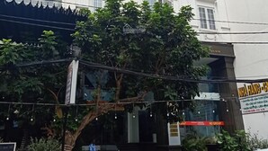 Um edifício com vários andares e fachada branca, com uma placa de 'T&T DANCESPORT' no andar térreo, e uma árvore na frente.