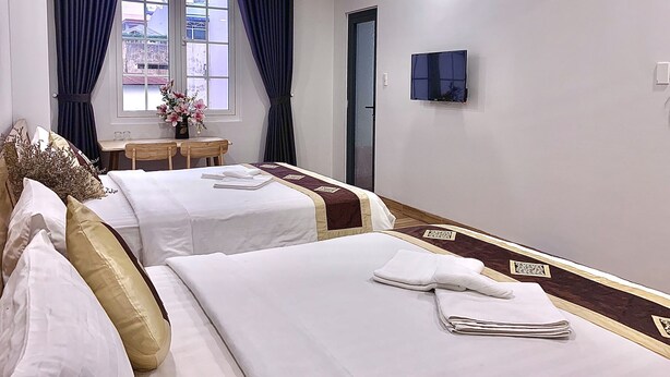 Quarto de hotel com duas camas, uma mesa pequena com um vaso de flores, uma televisão fixada na parede e um aparelho de ar condicionado.