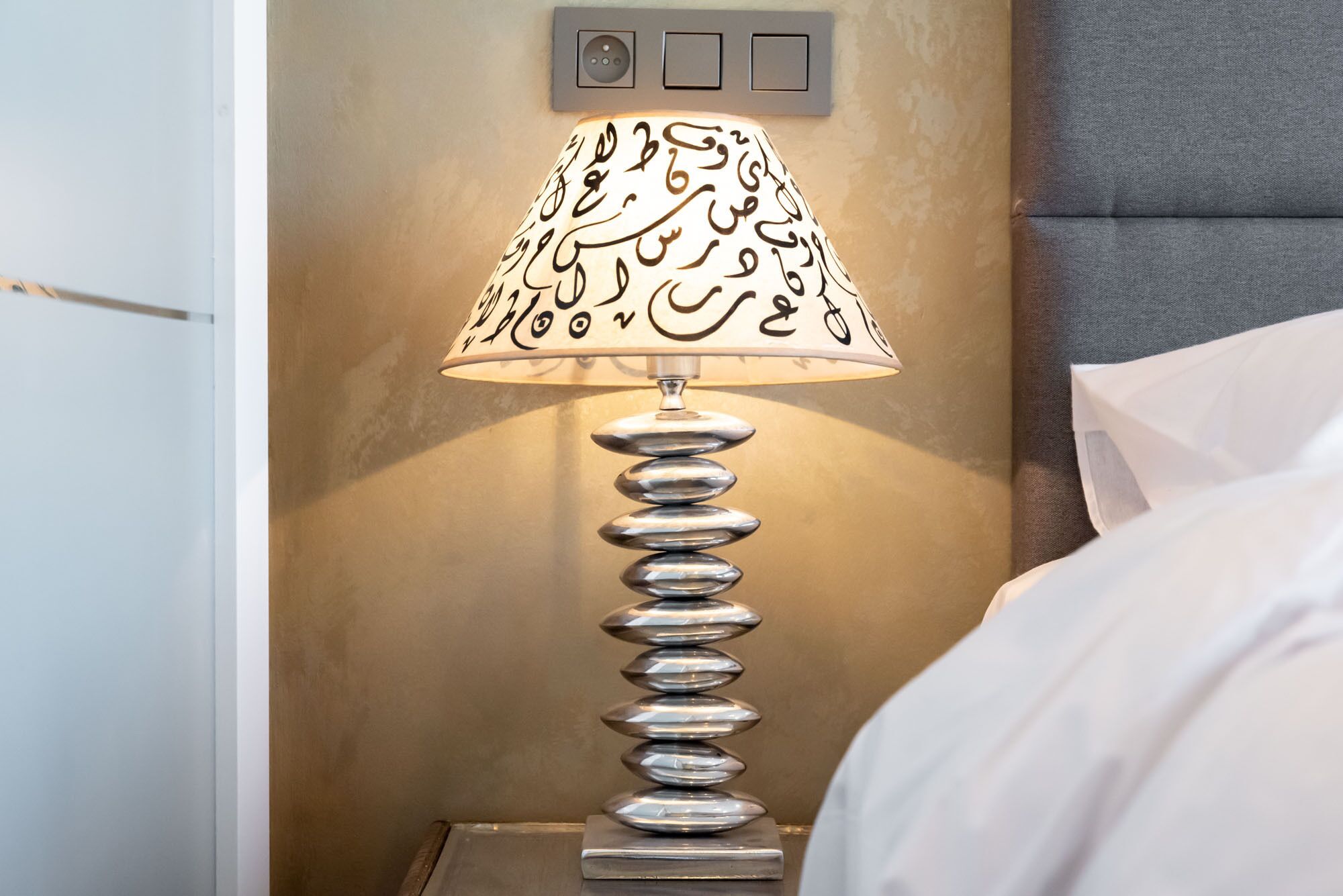 Uma luminária com cúpula estampada sobre uma mesa de cabeceira.