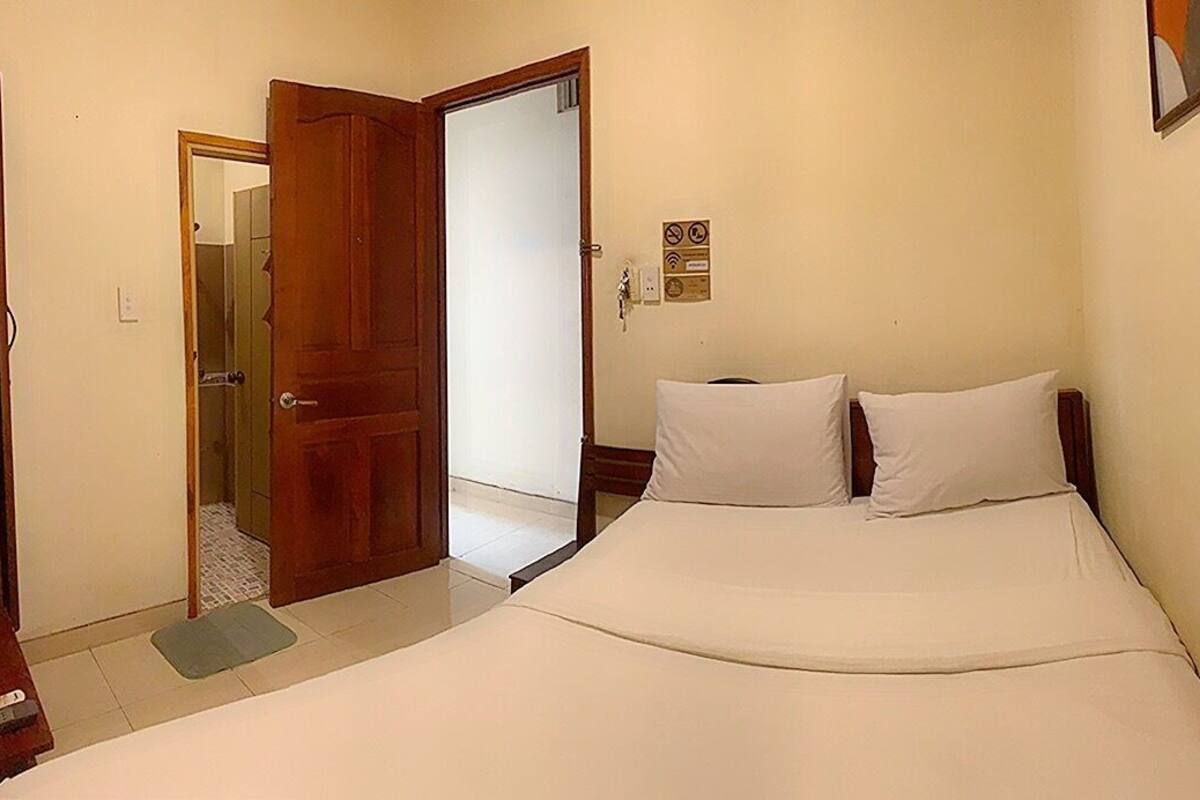 Quarto com cama, porta de madeira e um tapete pequeno no chão.