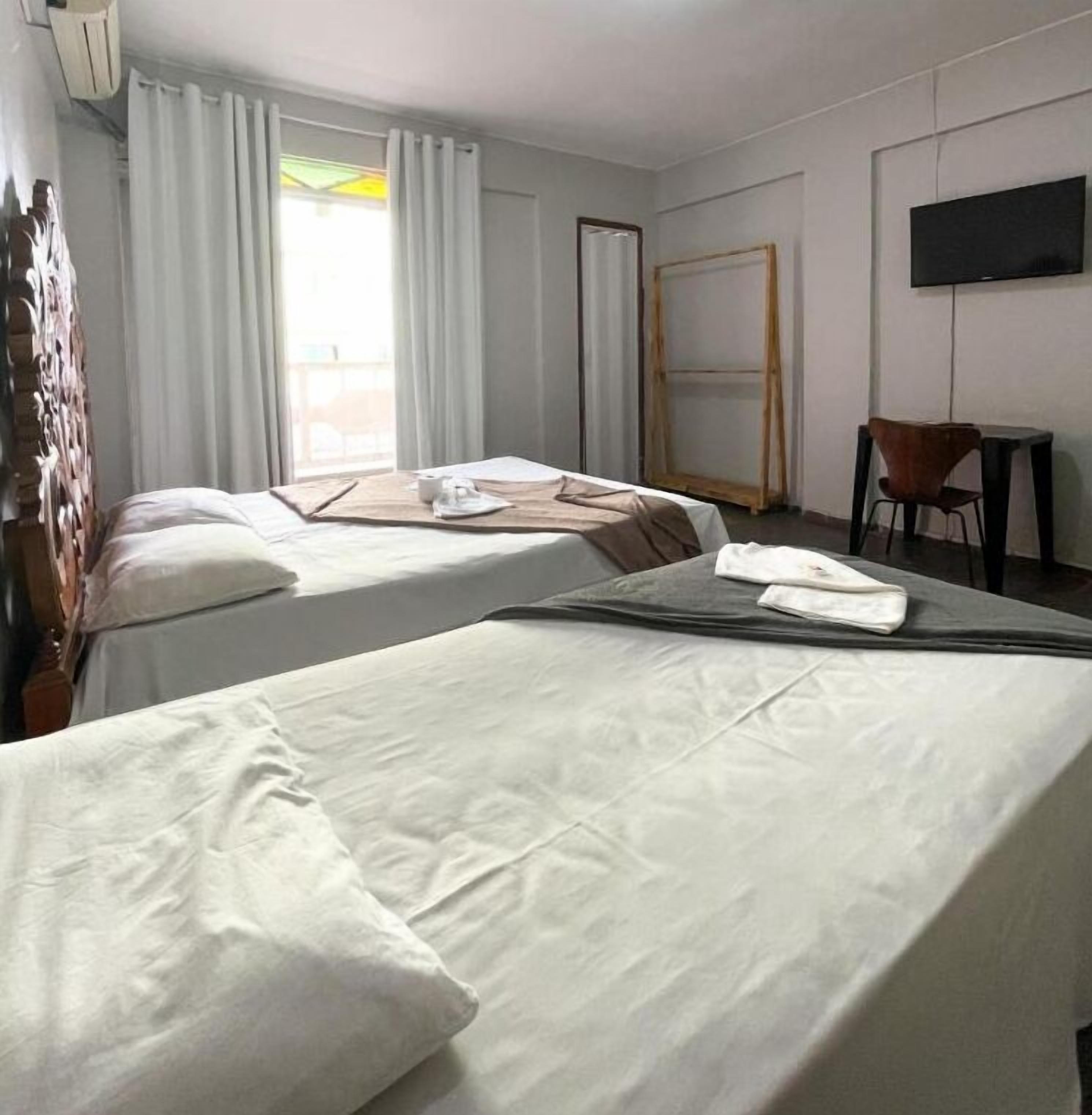Quarto de hotel com duas camas, televisão e janela com cortinas.