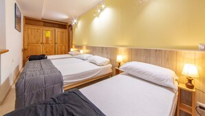 Quarto de hotel com duas camas, cabeceira de madeira, luminárias de cabeceira e guarda-roupa de madeira.