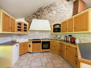 Cozinha com armários de madeira, parede de pedra, fogão a gás, micro-ondas e cafeteira.