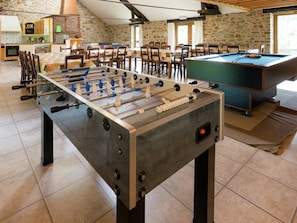 Um quarto com mesa de futebol, mesa de bilhar e área de refeições com cadeiras e mesa.