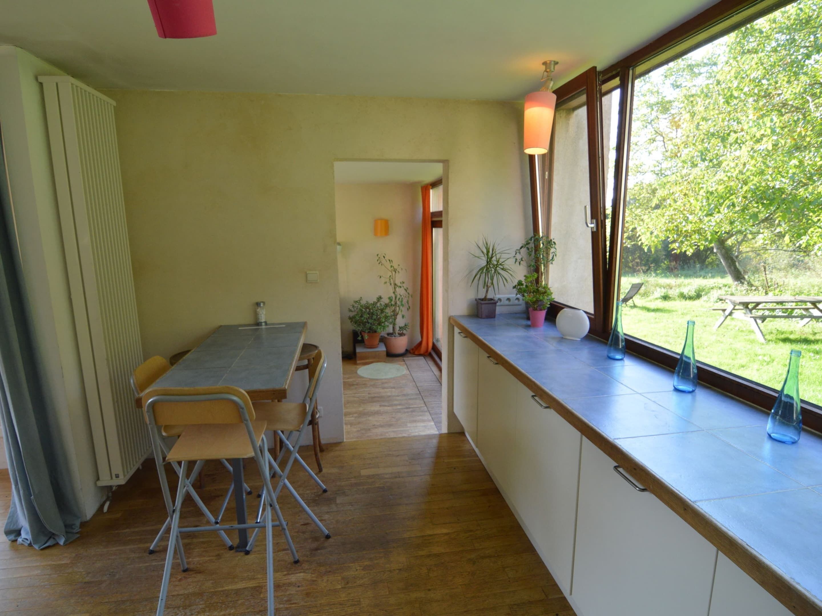 Uma cozinha com mesa de jantar, cadeiras, plantas em vasos e vista para o jardim.