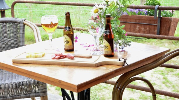 Uma mesa de madeira com uma garrafa de cerveja, um copo e uma tábua de carne.