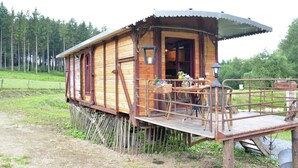 Uma cabana de madeira com varanda, guarda-corpo de metal e uma pequena mesa com cadeiras.
