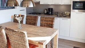 Uma cozinha moderna com armários brancos, mesa de jantar de madeira, cadeiras de vime e eletrodomésticos de aço inoxidável.