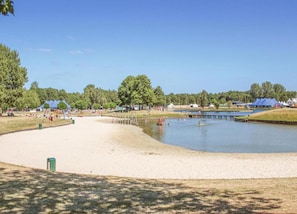 Um parque à beira do lago com uma praia de areia, um cais e tendas ao fundo.