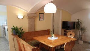 Uma sala de jantar com mesa de madeira e bancos, uma televisão e um vaso de planta.