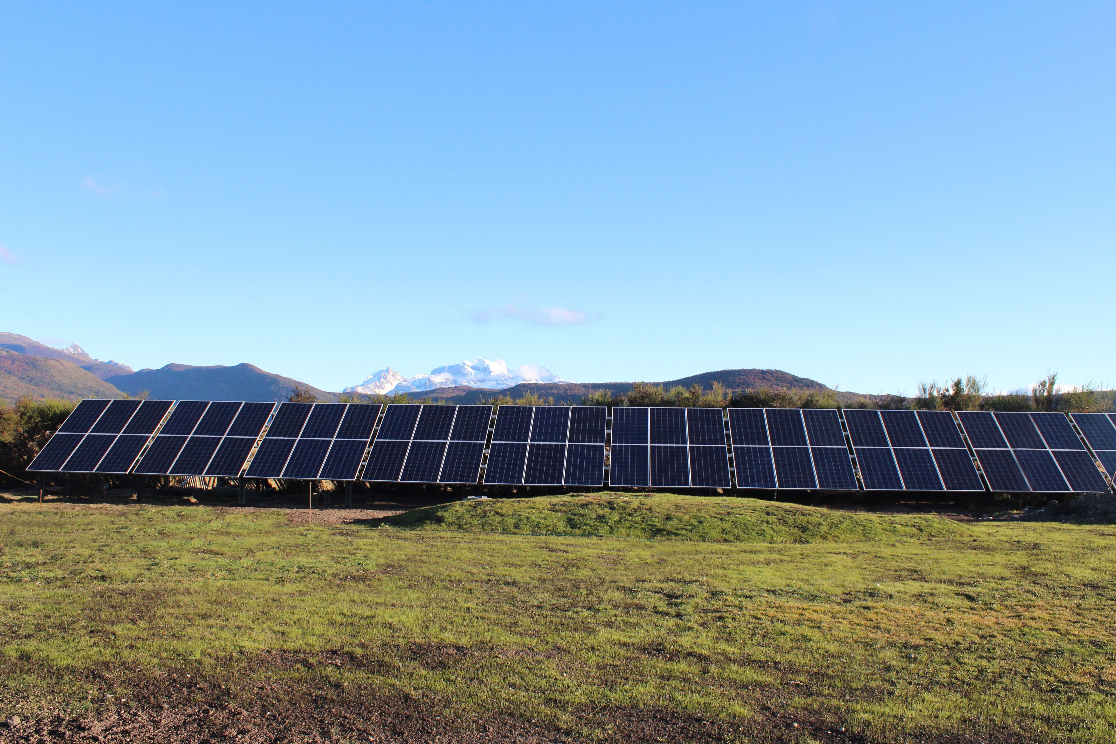 Uma fazenda solar com fileiras de painéis solares em um campo gramado, com montanhas ao fundo.