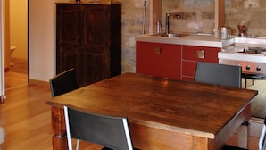 Uma cozinha com uma mesa de madeira, cadeiras, um fogão e uma parede de pedra.