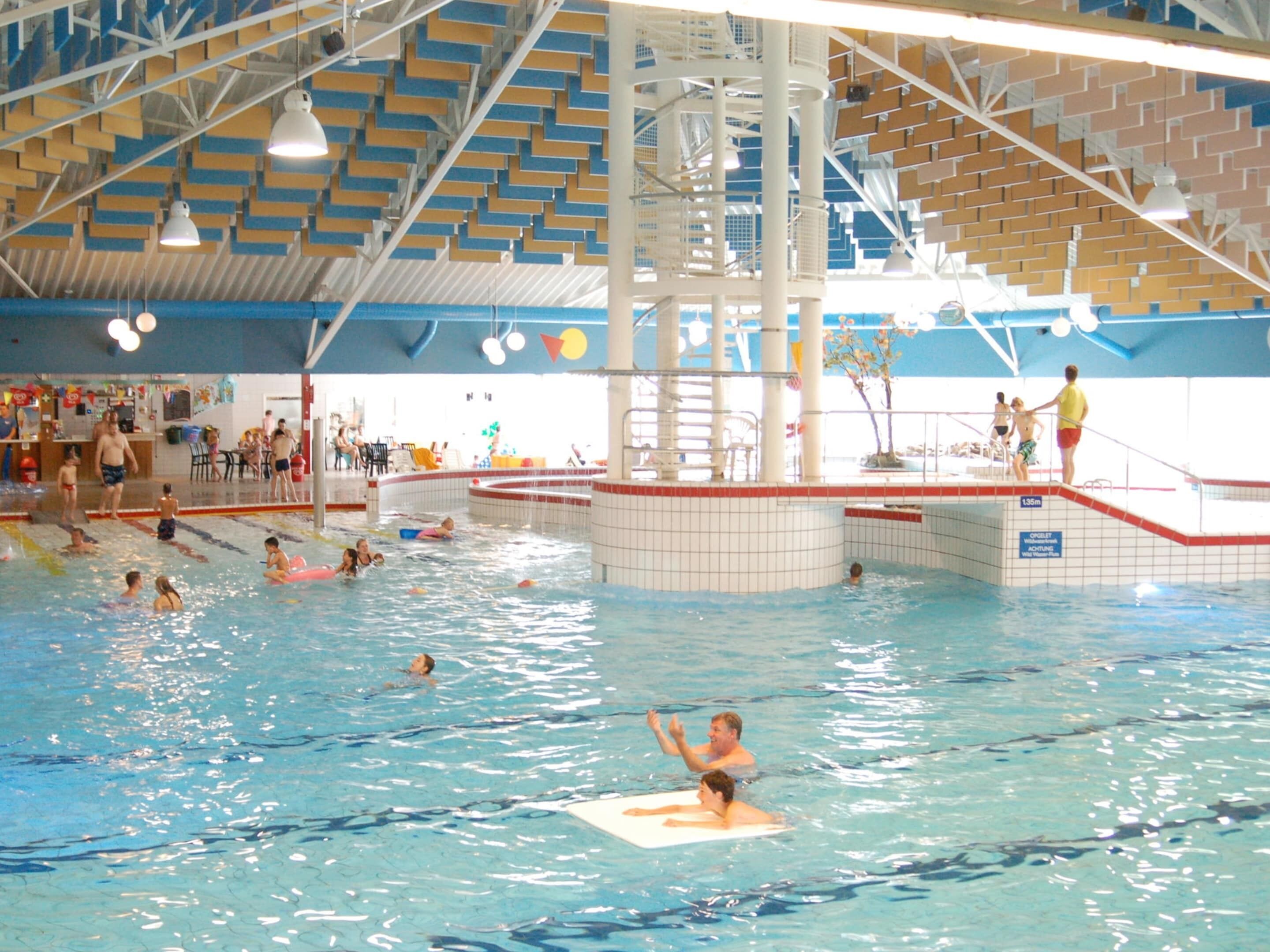 Piscina interior com várias pistas de natação, plataforma de mergulho e área para espectadores.