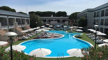 Piscina cercada por espreguiçadeiras e guarda-sóis, com um edifício ao fundo.