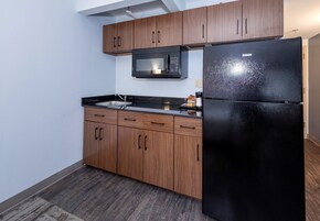 Cozinha compacta com armários de madeira, geladeira preta, micro-ondas e pia.