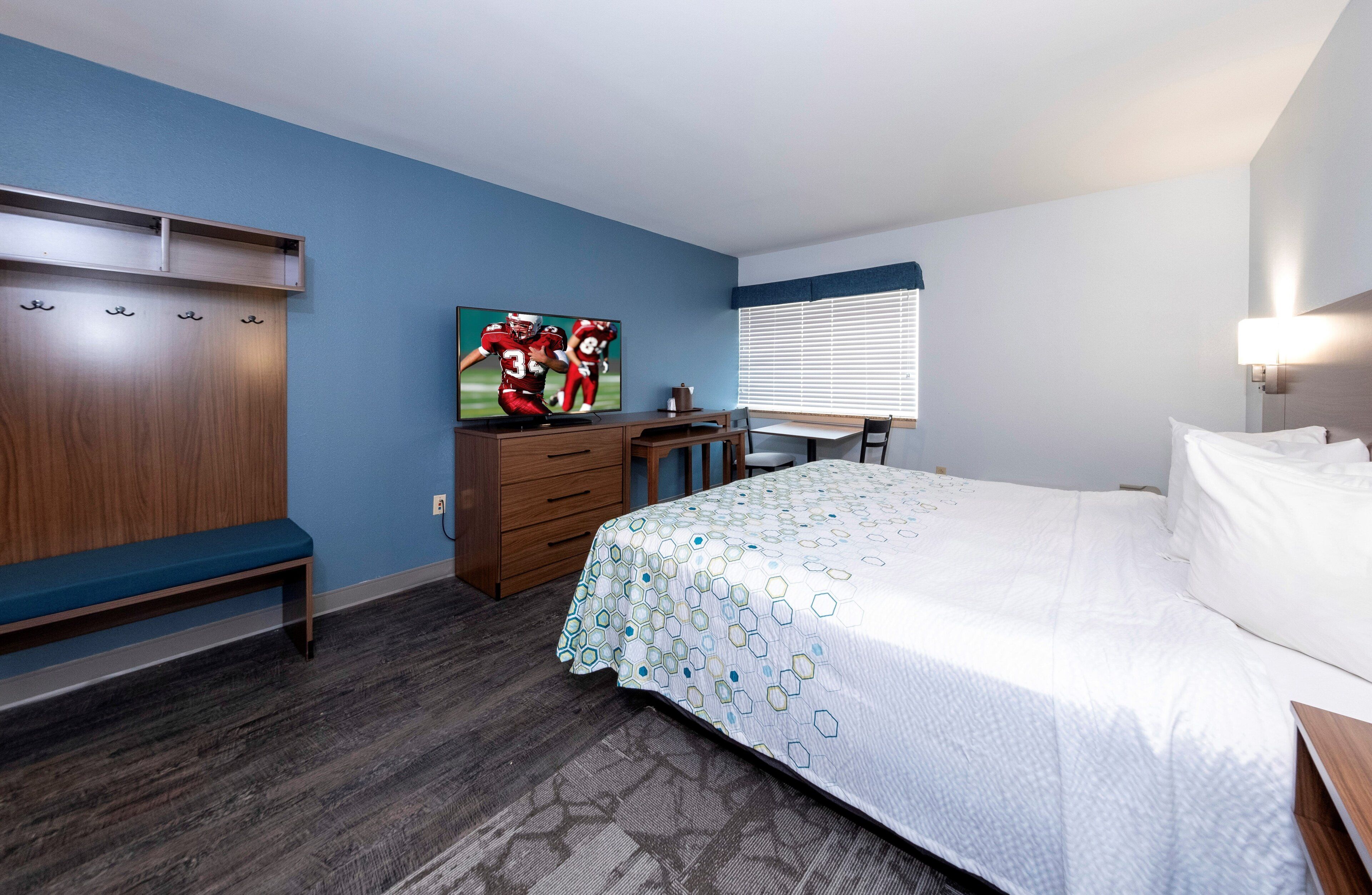Quarto de hotel com cama, escrivaninha, cadeira, armário e um quadro na parede.